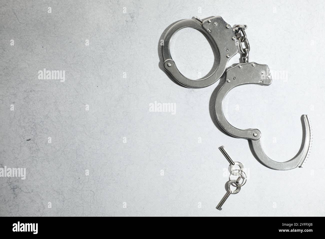 Metal chain handcuffs and keys on light grey table, top view. Space for ...