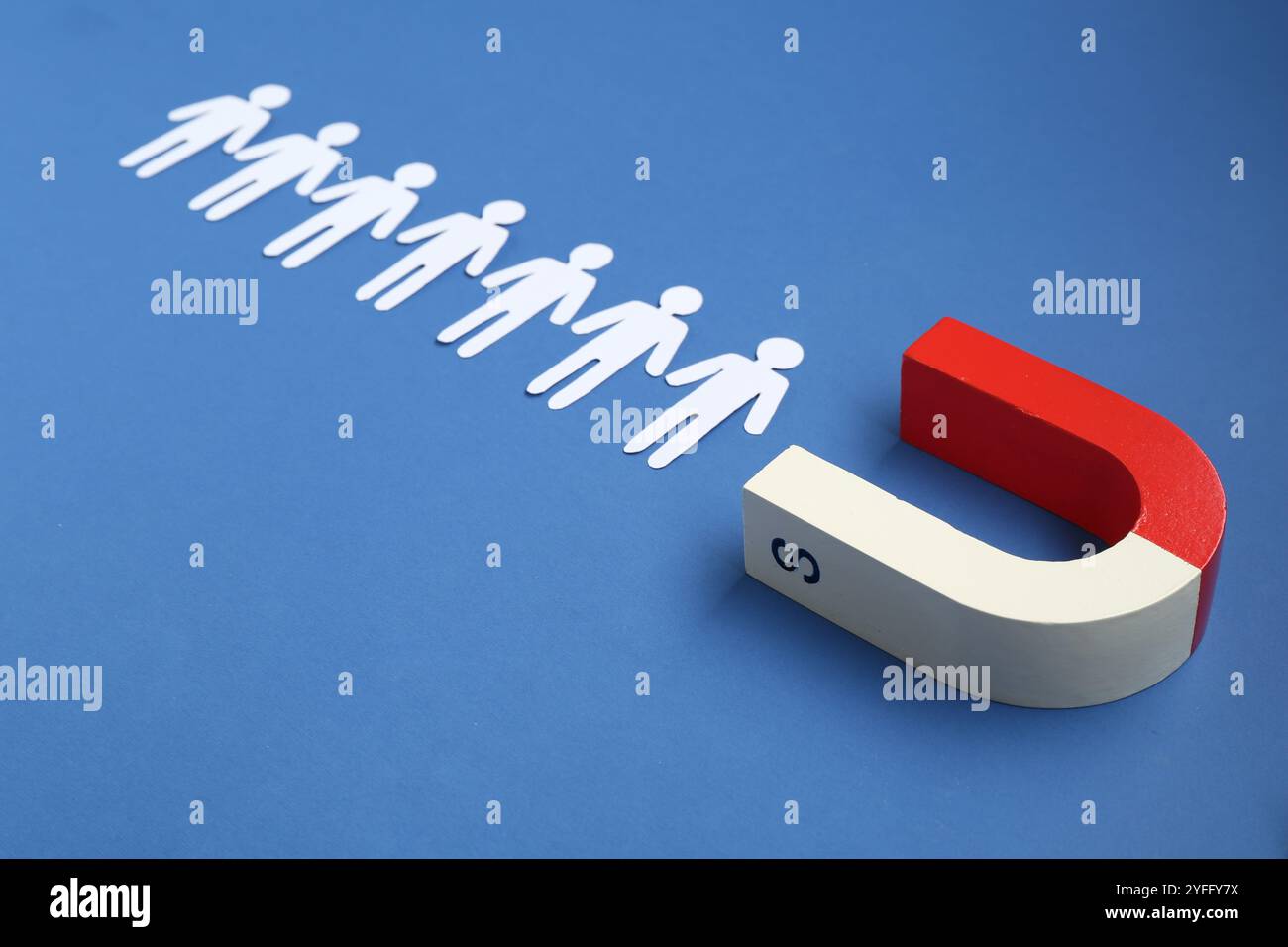 Magnet attracting paper human figures on blue background Stock Photo ...