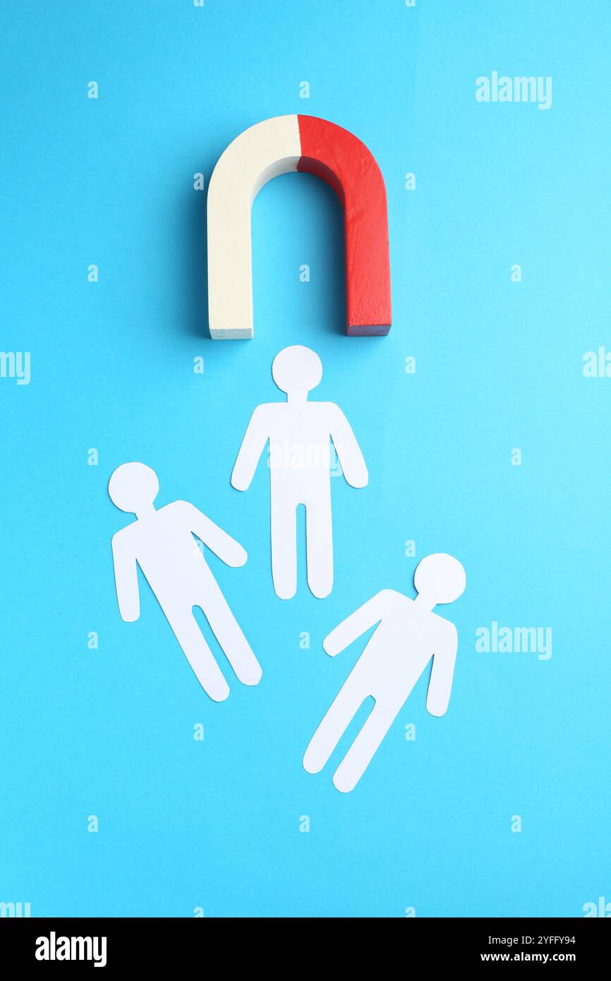 Magnet attracting paper cutouts of humans on light blue background ...