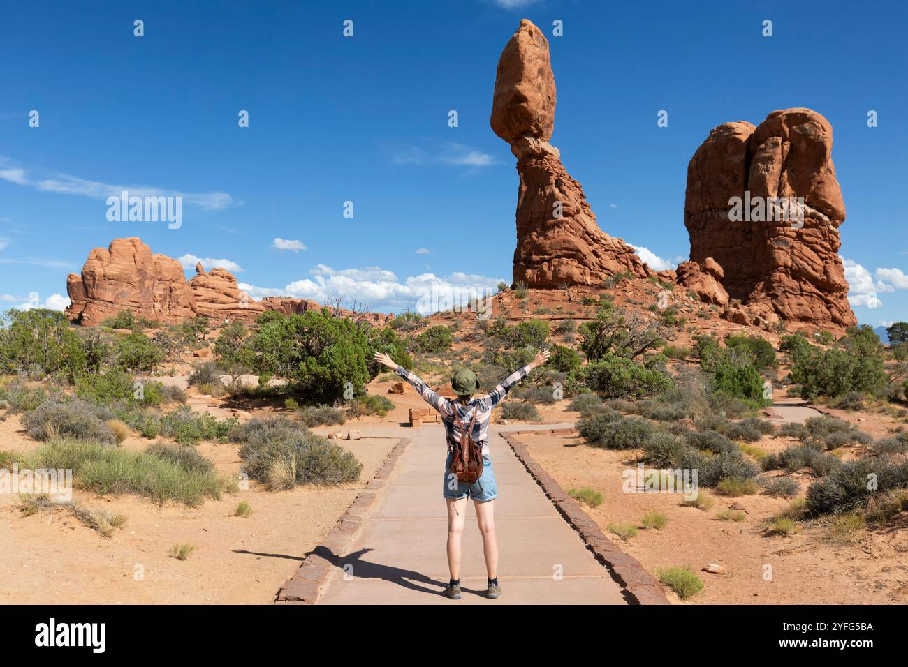 young tourist with arms up in front of balanced rock in arches national ...