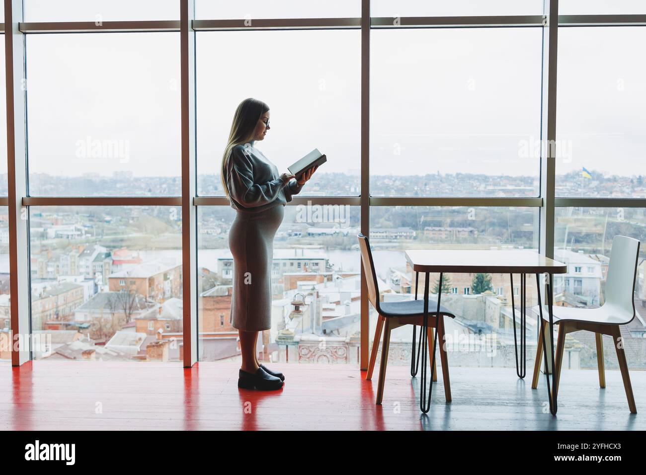 Young pregnant woman at work in the office standing near the window ...