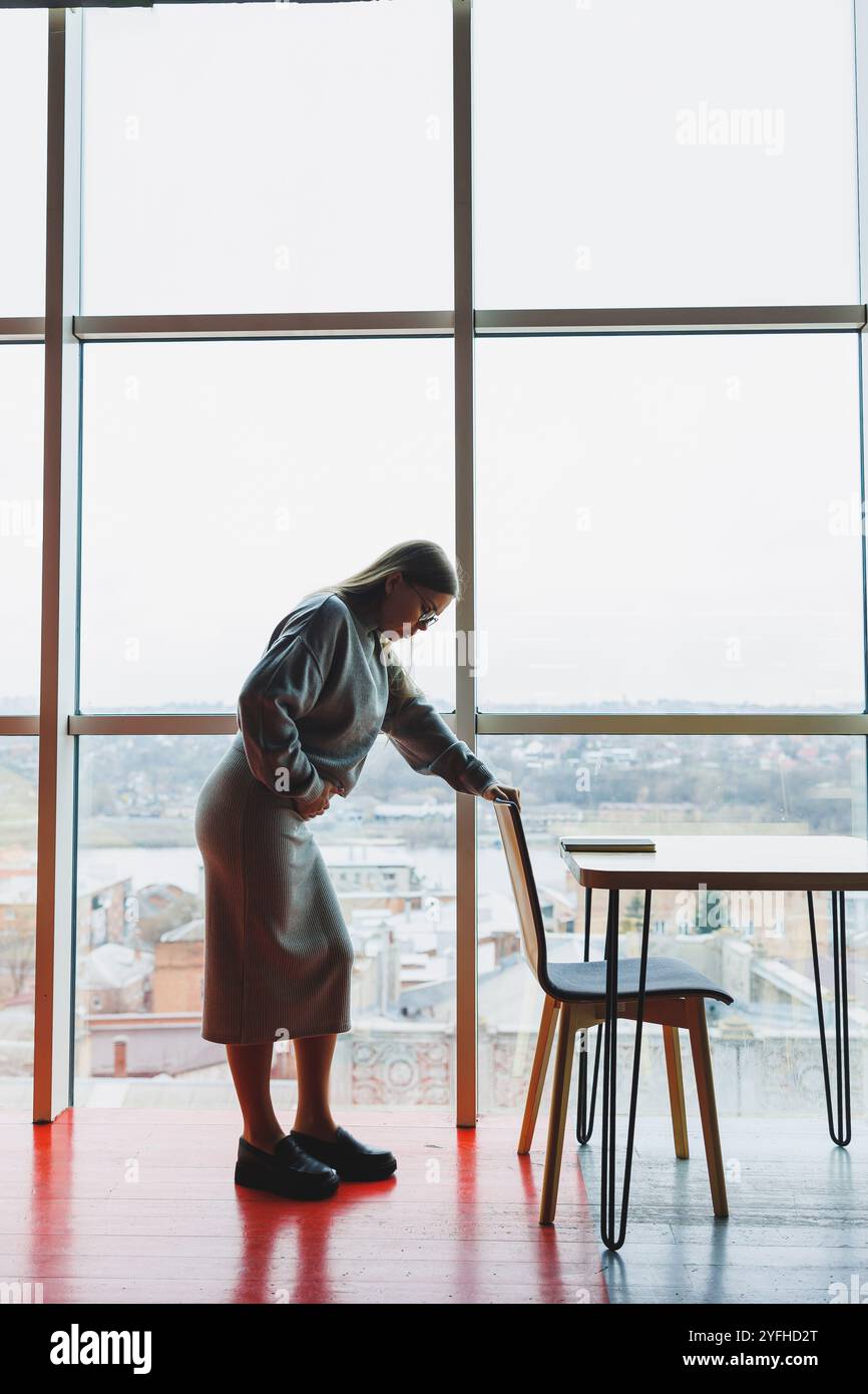Young pregnant woman at work in the office standing near the window ...