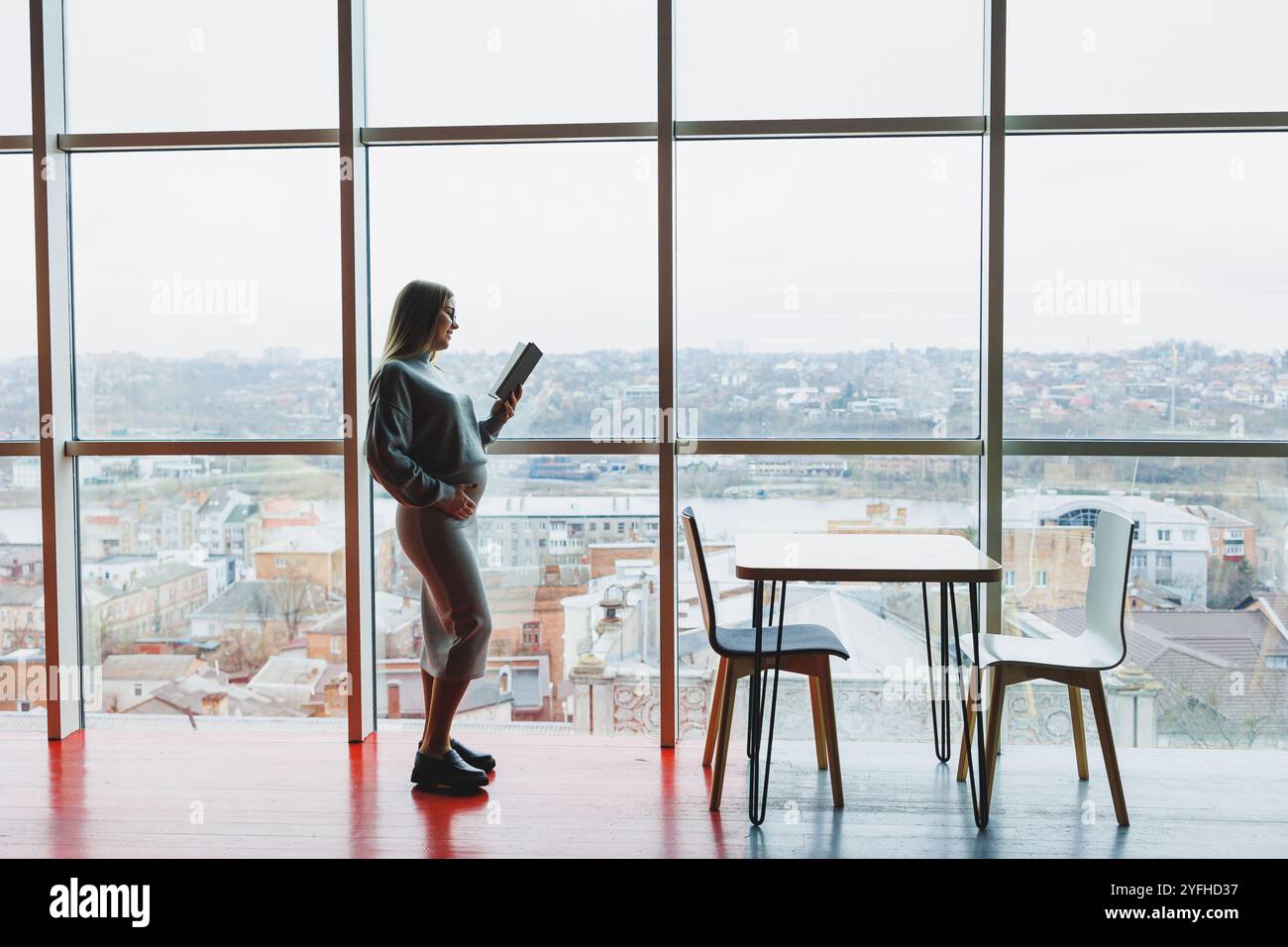 Young pregnant woman at work in the office standing near the window ...