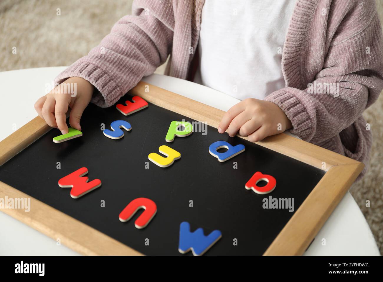 Little girl learning alphabet with magnetic letters at white table ...