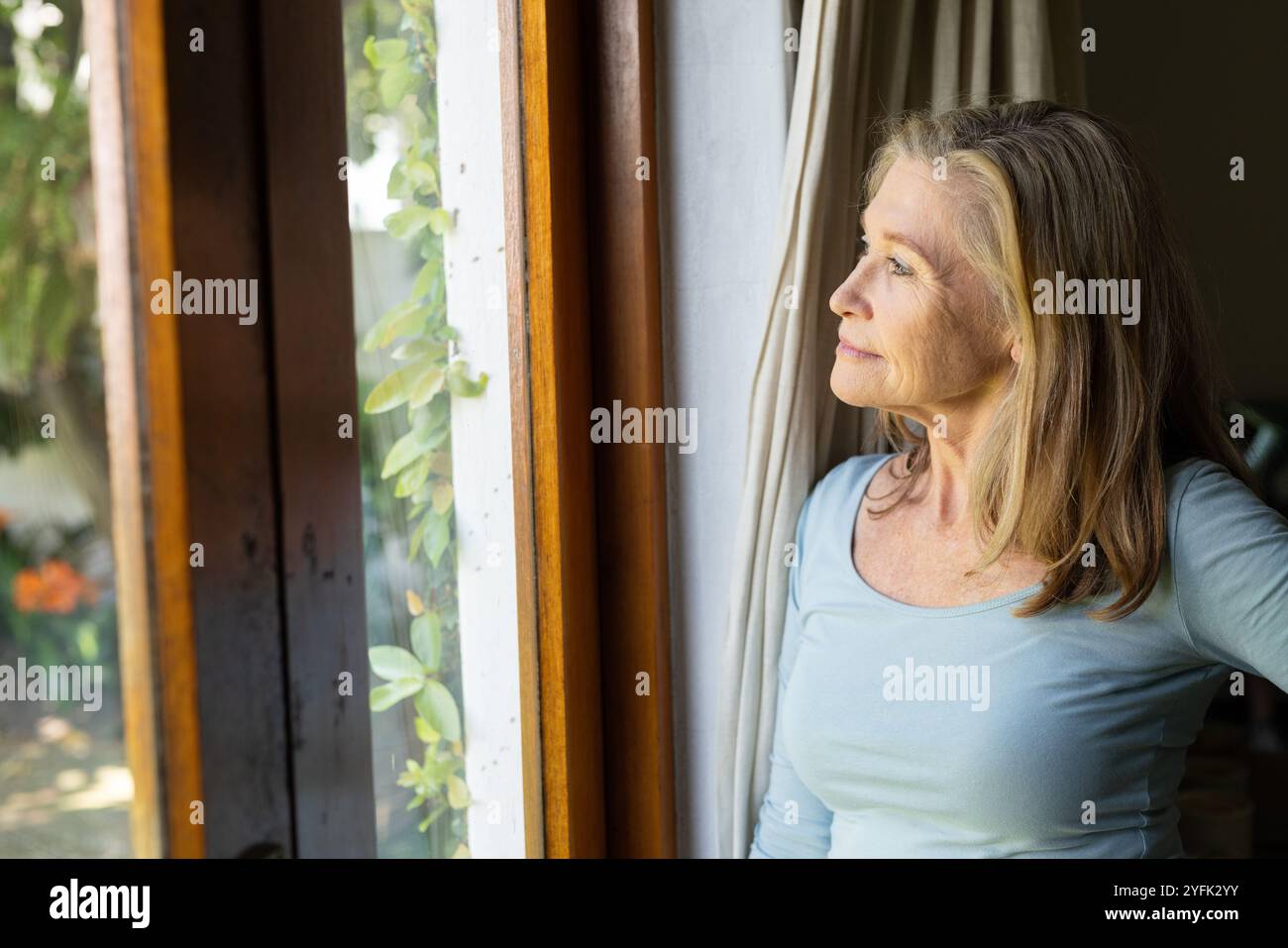 senior woman gazing out window, enjoying peaceful moment at home ...