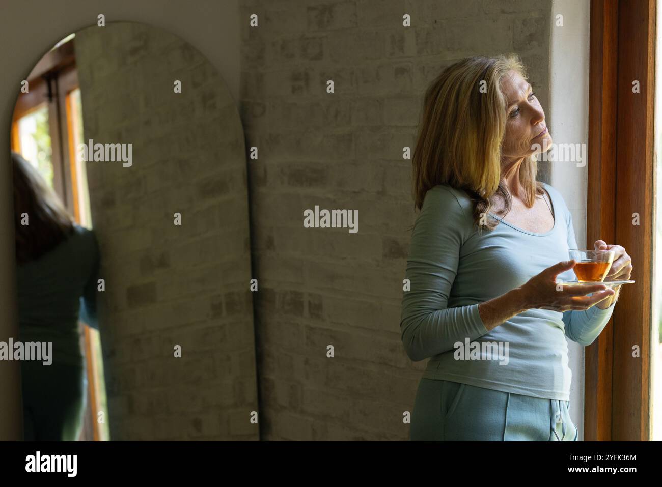 senior woman enjoying tea by window, reflecting peacefully at home ...