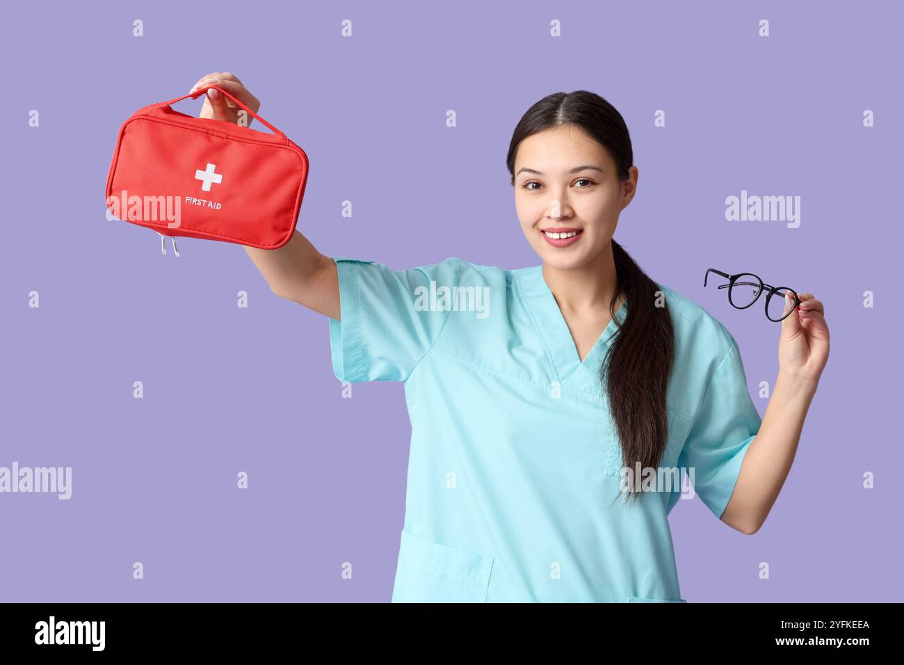 Asian female doctor with first aid kit and eyeglasses on lilac ...