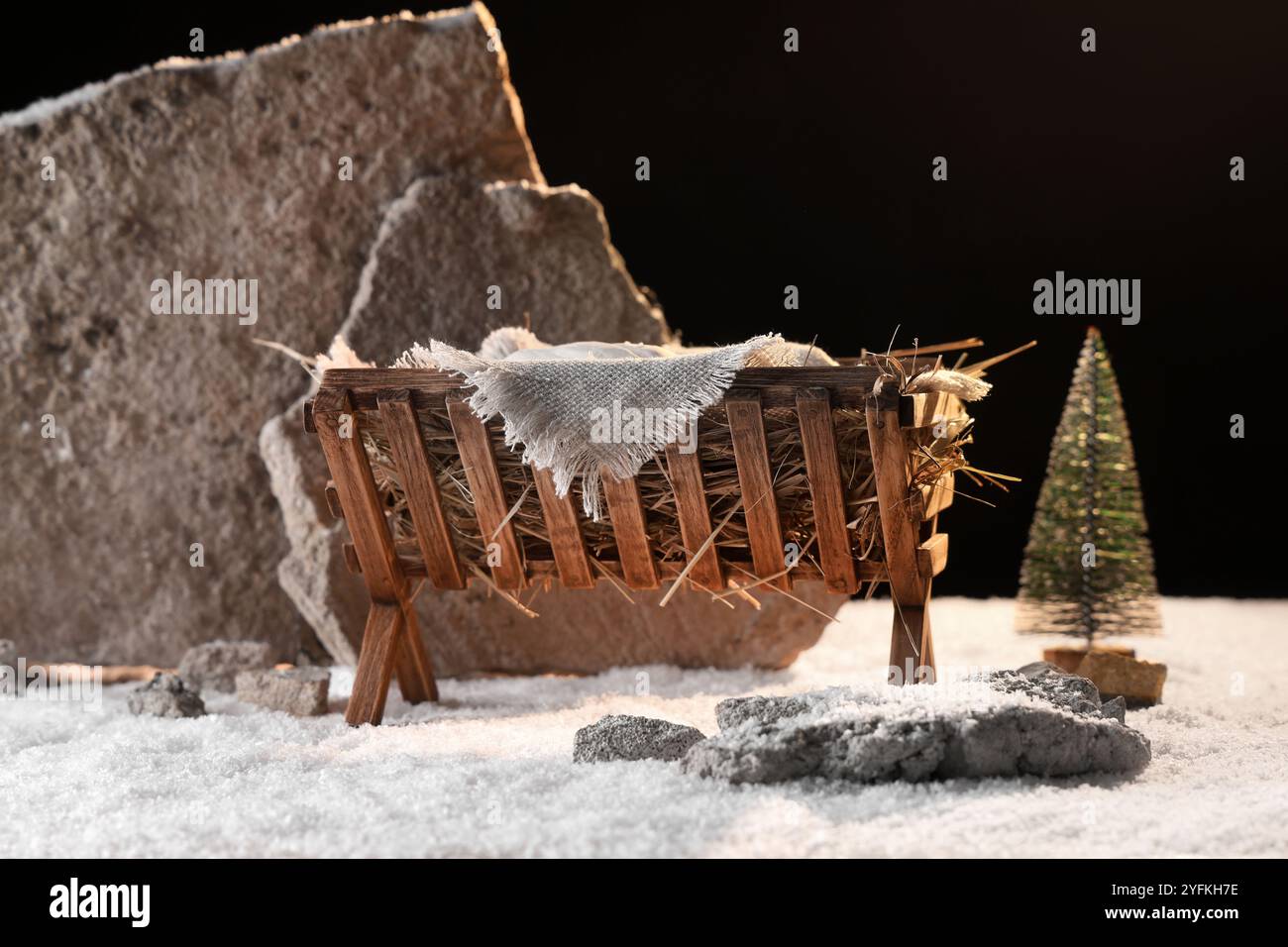 Manger with baby Jesus, rocks and Christmas tree on snow against dark ...