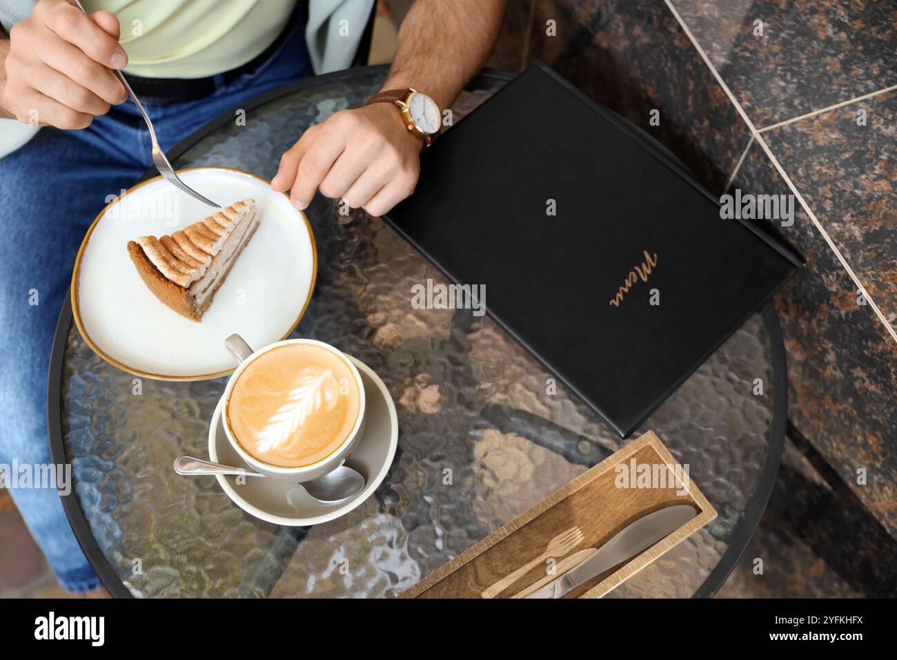 Young man with menu eating cake at table in street cafe, top view Stock ...