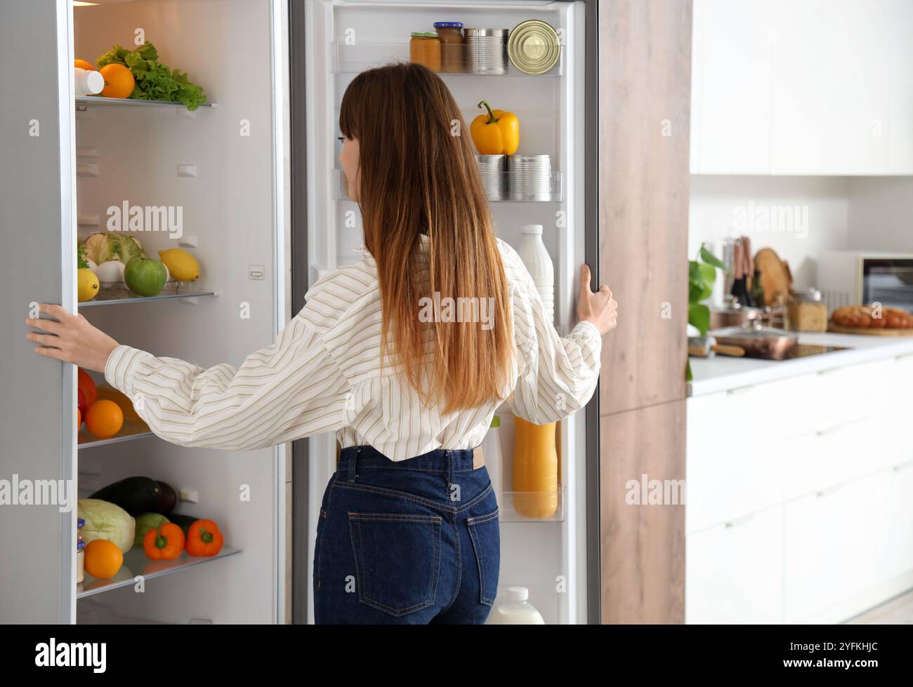Young woman opening fridge in kitchen, back view Stock Photo - Alamy