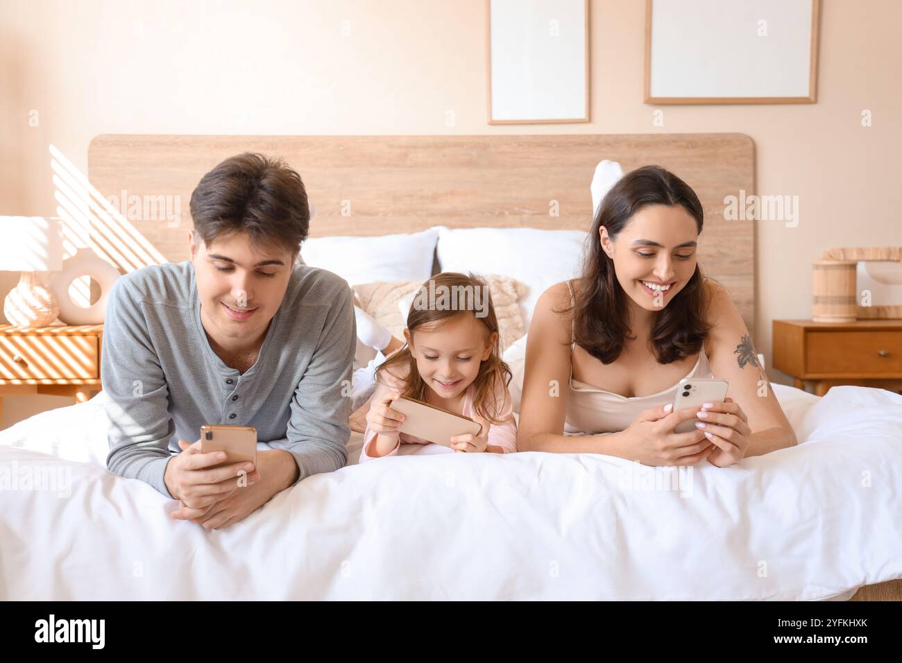 Little girl with her parents using mobile phones in bedroom Stock Photo ...