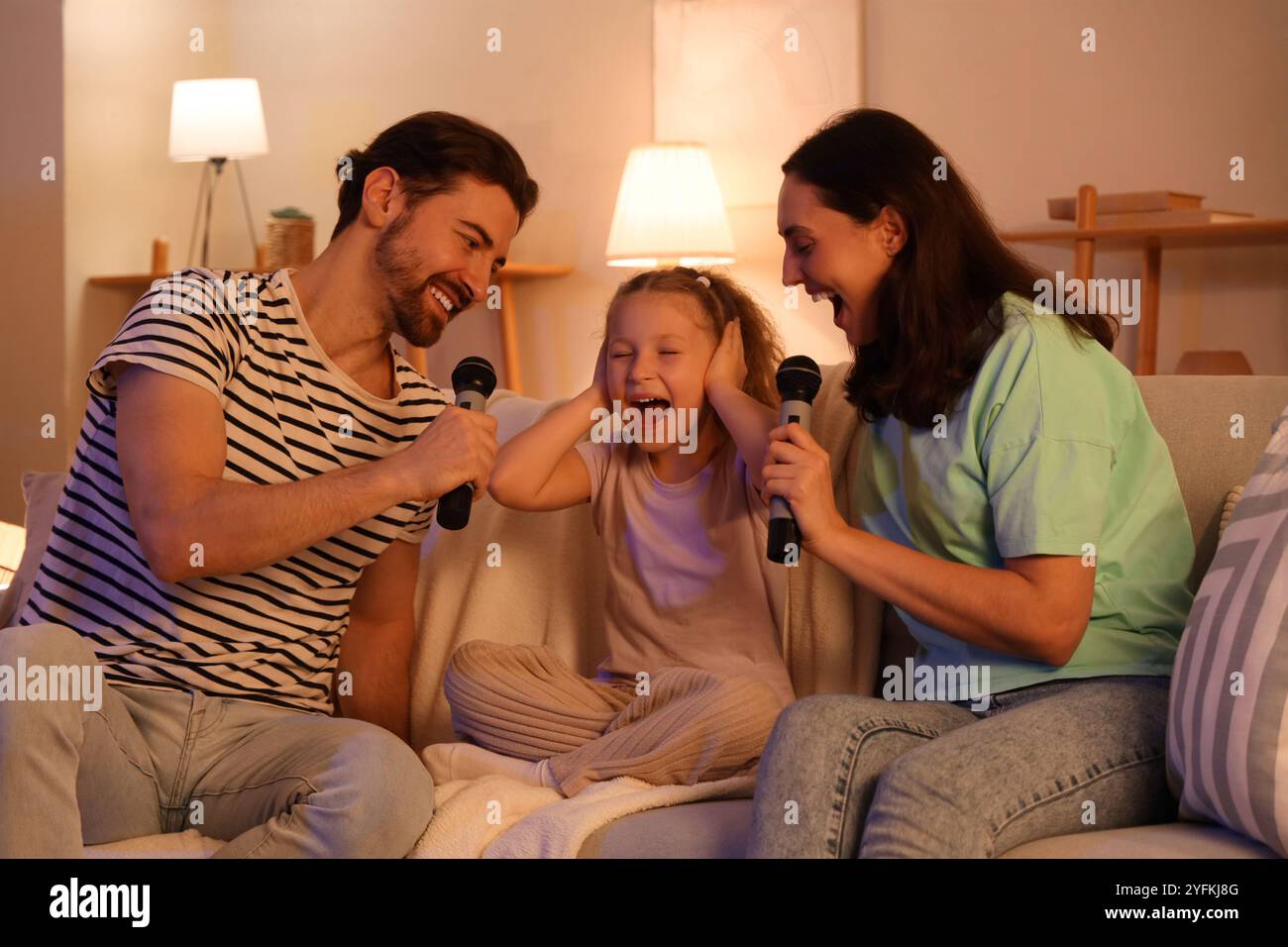 Happy family with microphones singing karaoke on sofa at home in ...