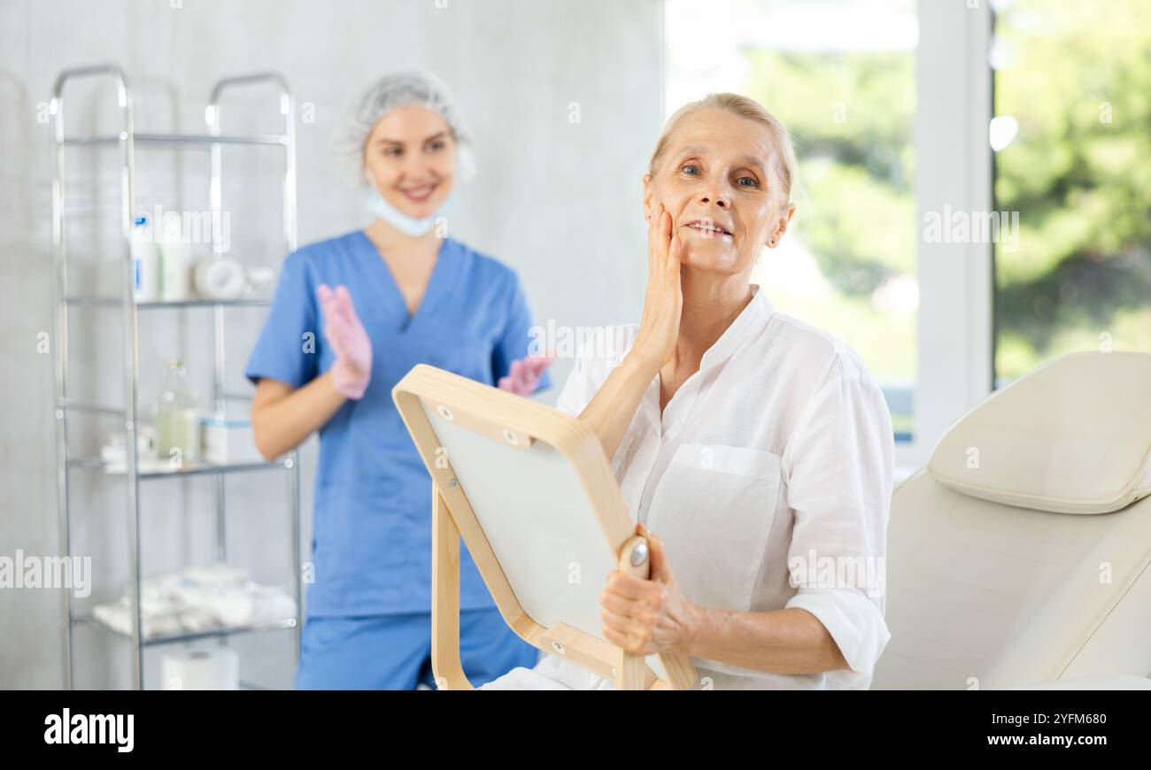 Satisfied old woman patient holding mirror sitting on clinical chair ...