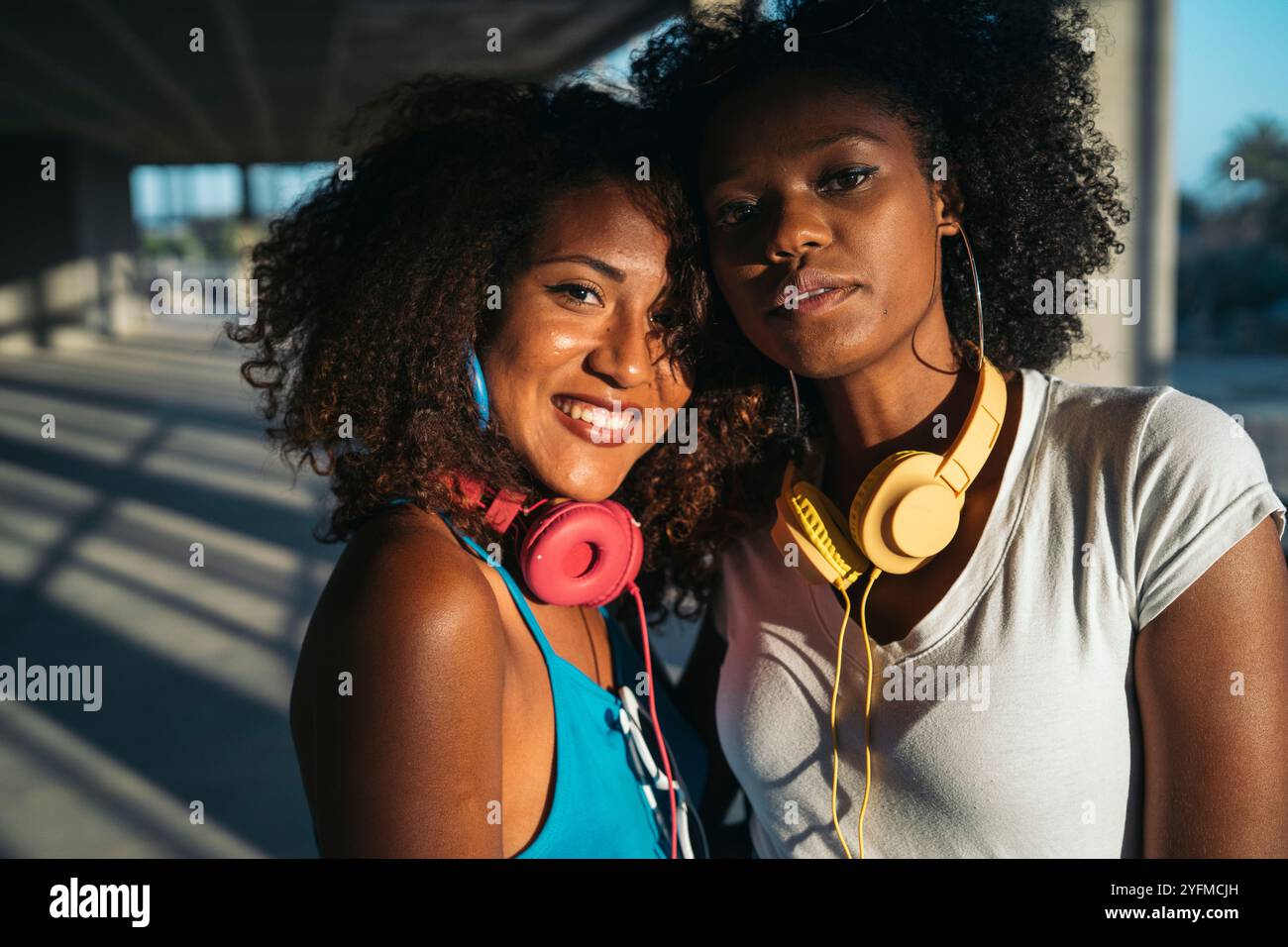 Two young women wearing headphones smiling under bridge Stock Photo - Alamy