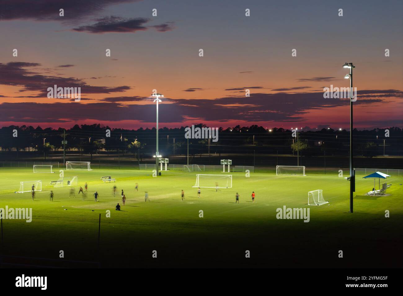 Public sports stadium with young people playing football game at sunset ...