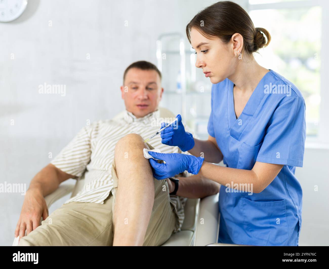 Female doctor performs intra-articular injection treatment of knee ...
