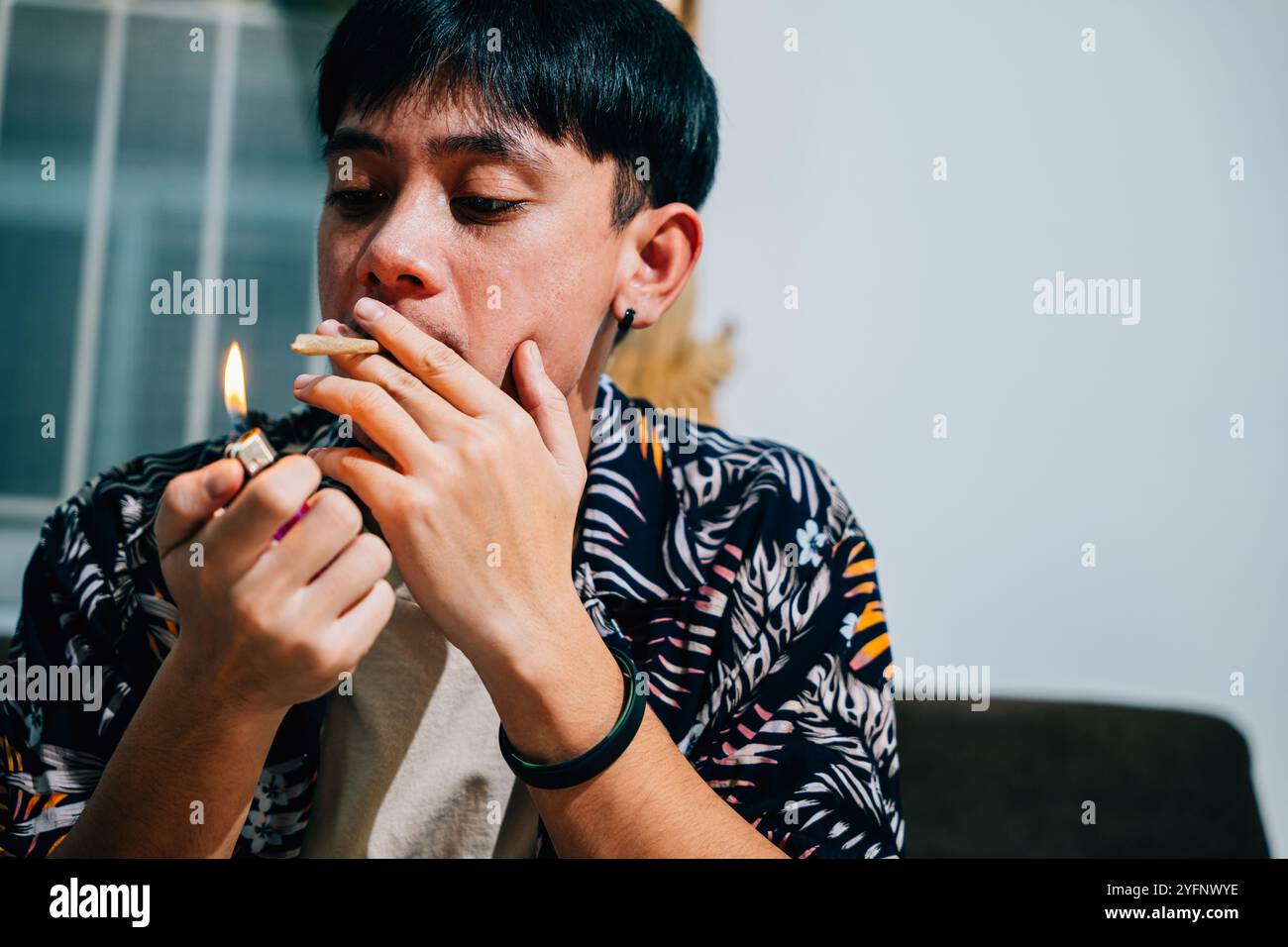 Asian young man smoking a cigarette while sitting on a couch joint ...