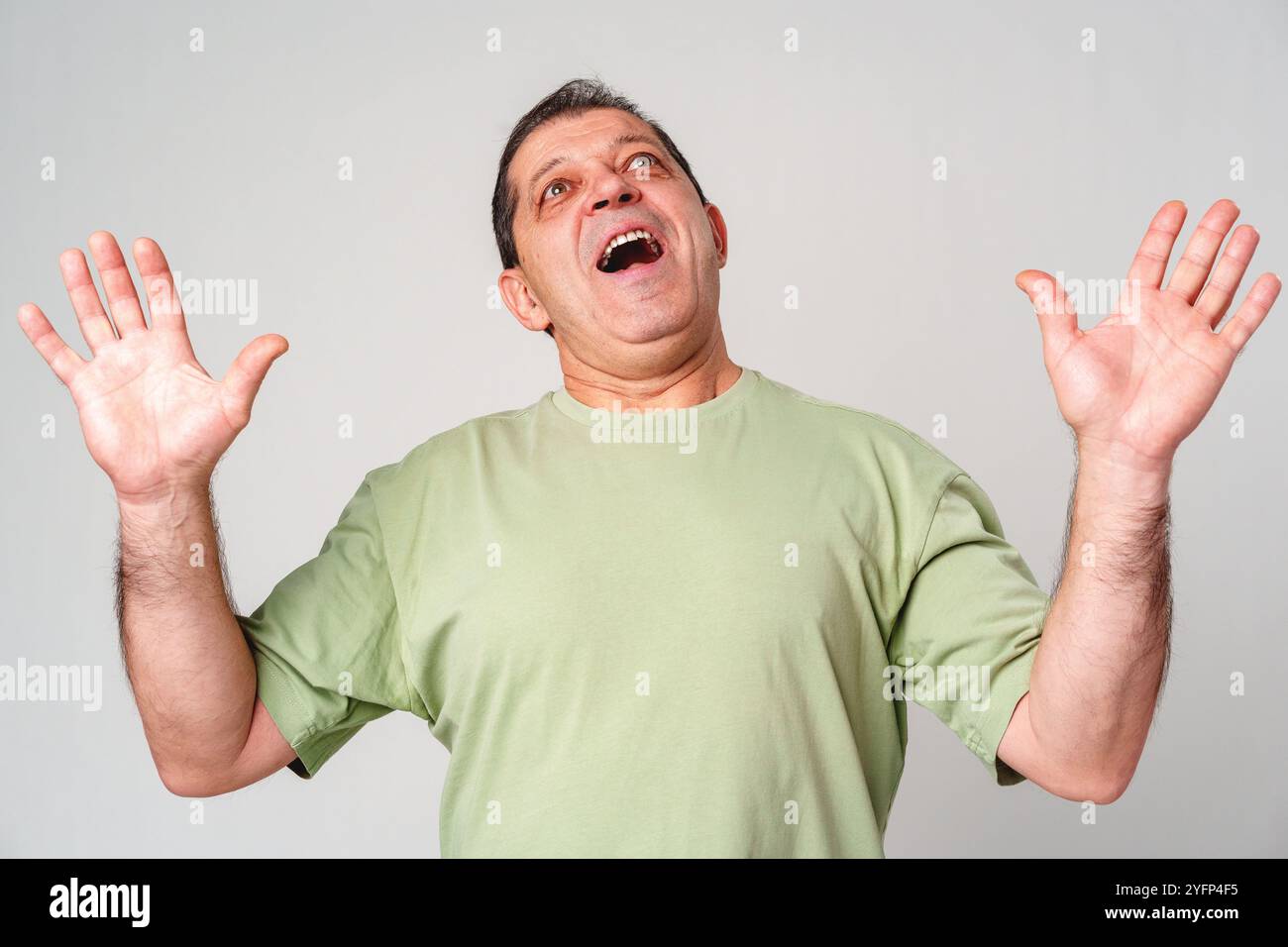 A middle-aged man with a neutral expression raises his hands in a ...