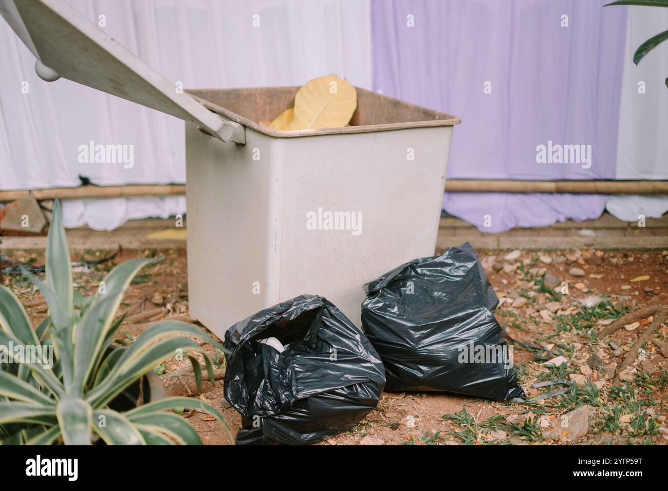 A garbage bin with two black trash bags placed beside it, ready for ...