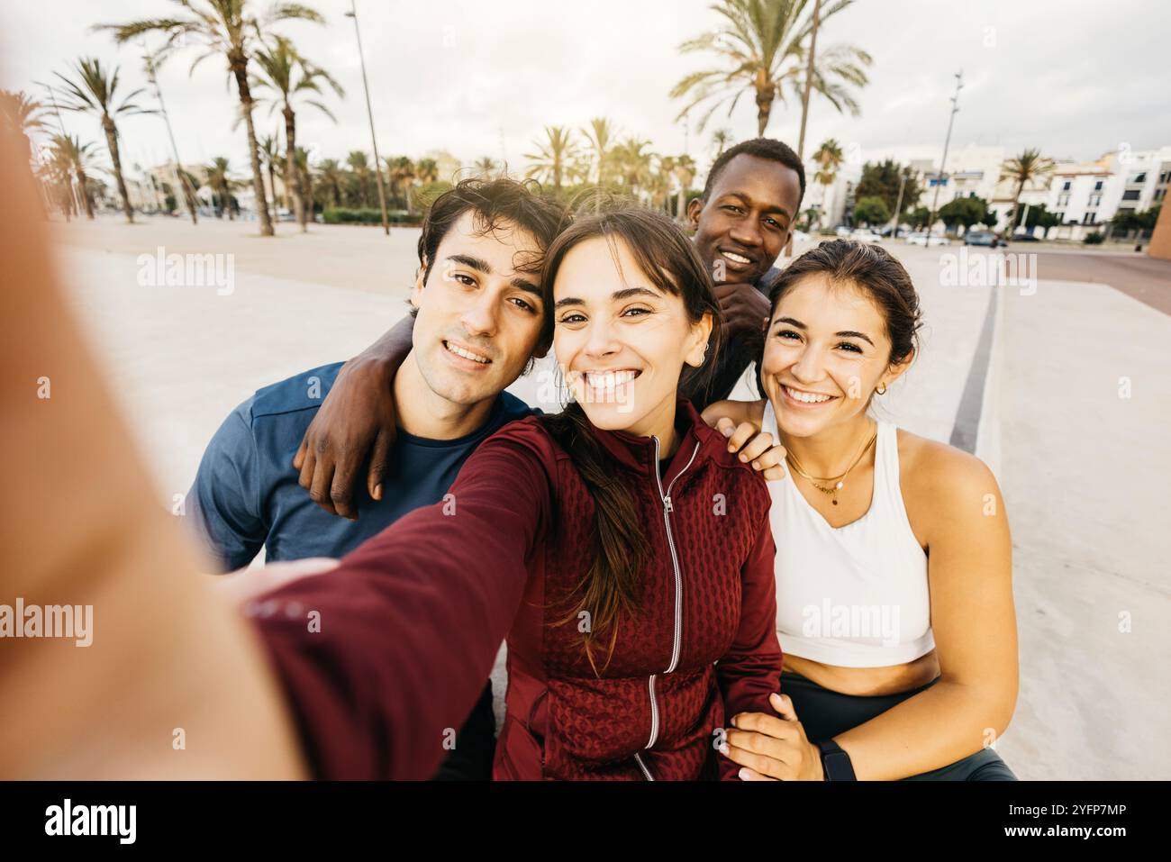 A group of cheerful friends pose for a selfie in a sunny park after a ...