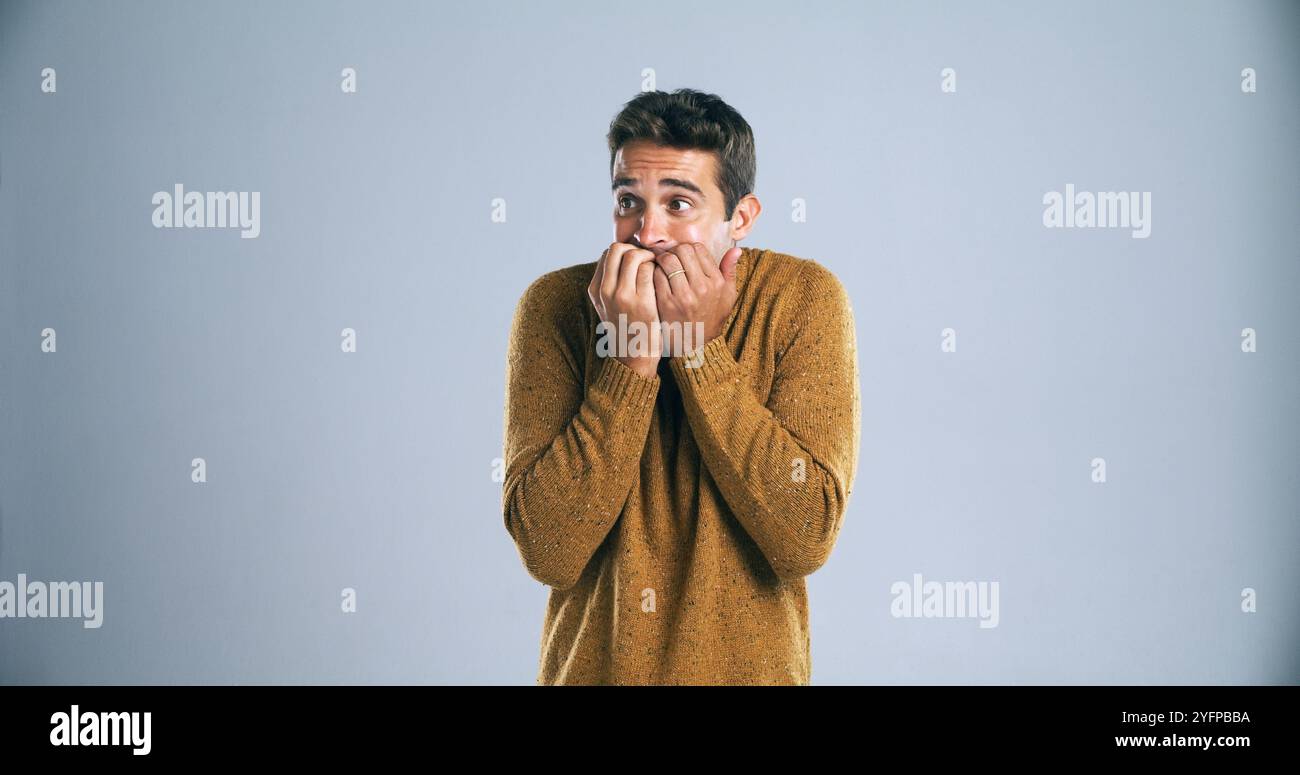 Scared, man and biting nails with fear in studio for horror, terror and panic for danger on ...