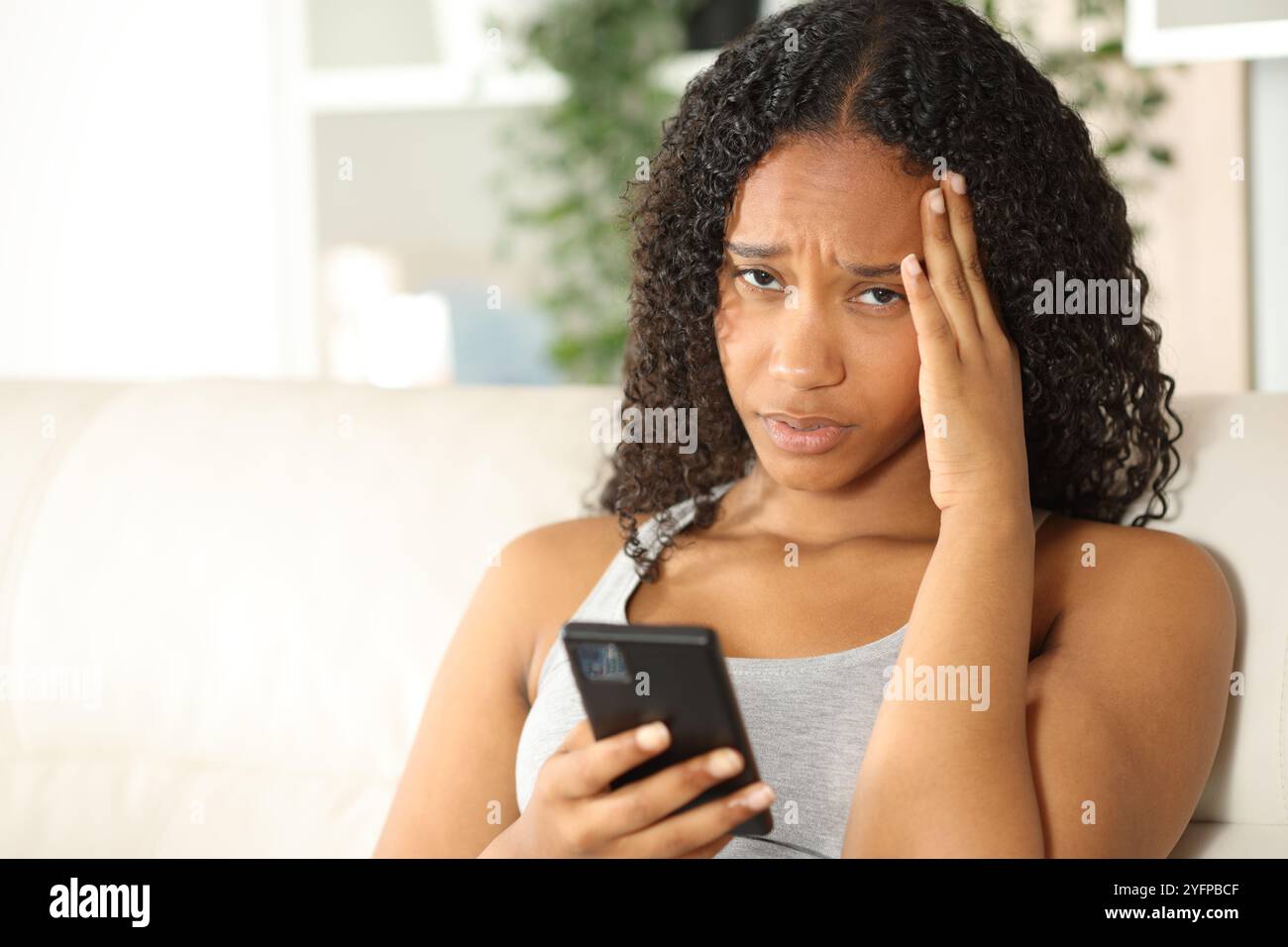 Worried black woman holding phone looking at camera at home Stock Photo - Alamy