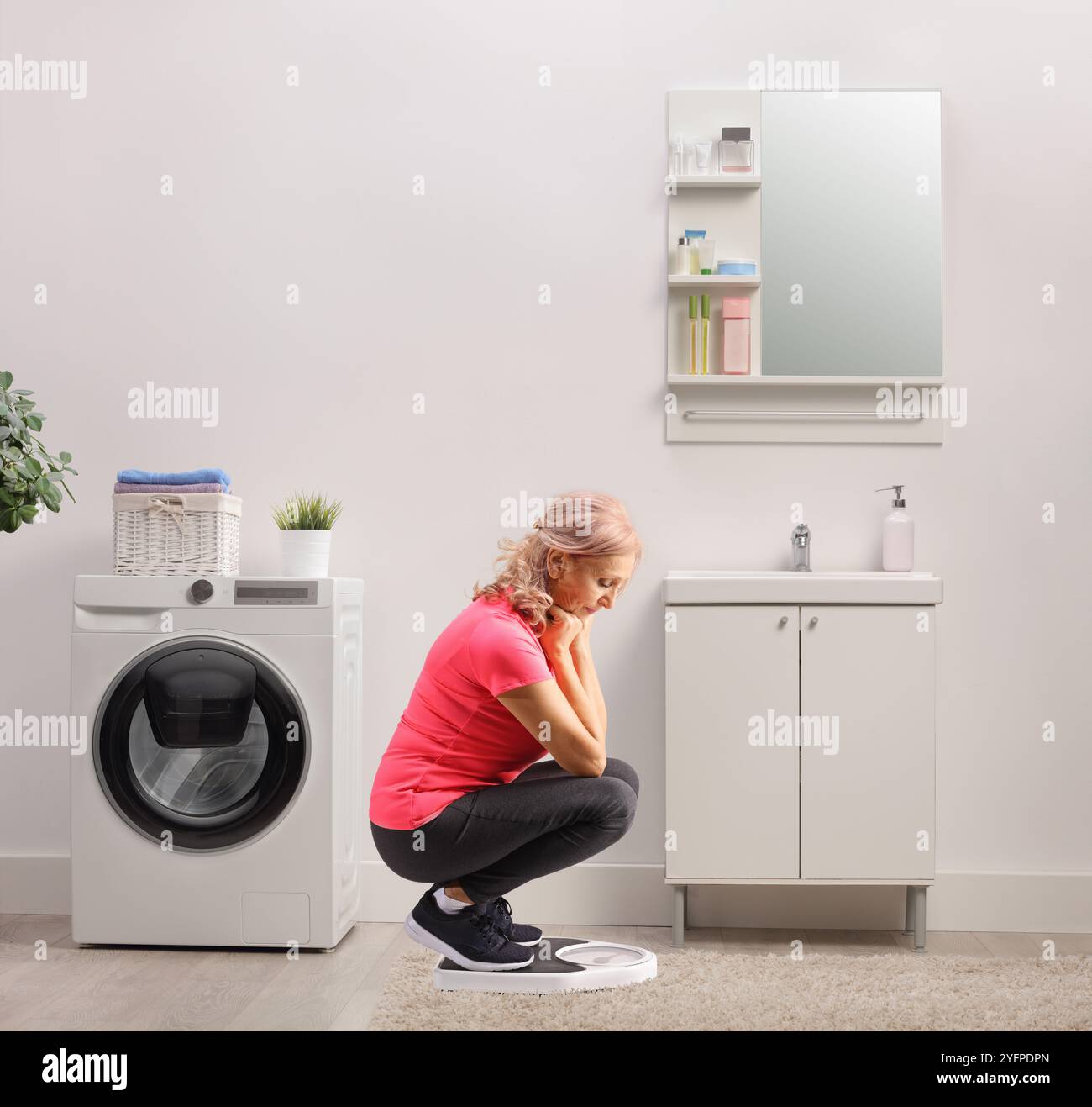Sad middle aged woman weighing on a scale in a bathroom Stock Photo - Alamy
