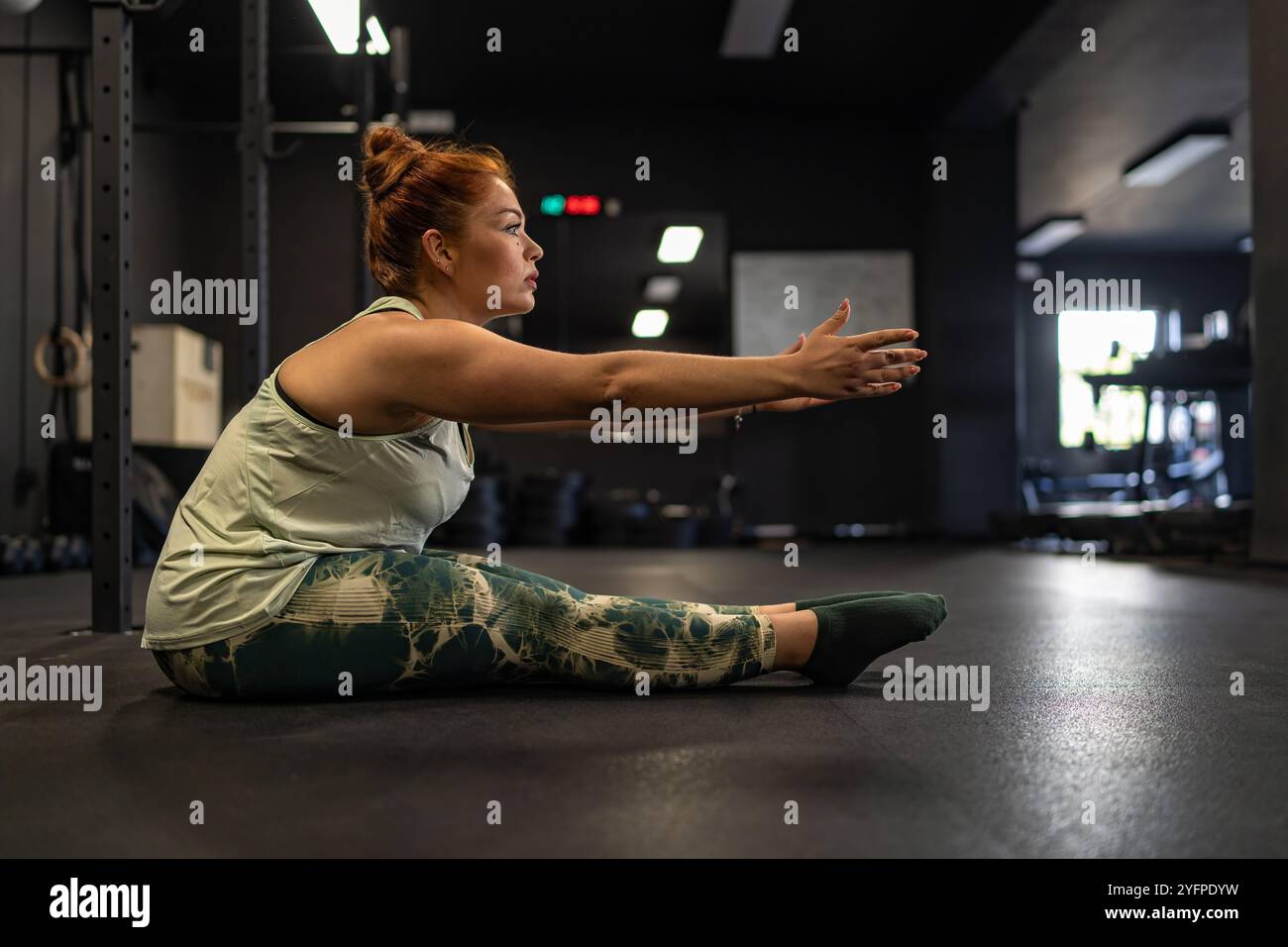 Athletic redhead woman performing stretching routine in contemporary ...