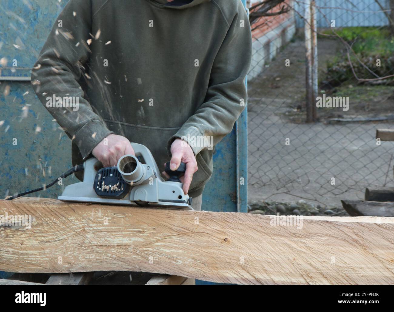carpenter with electric plane sanding surface of wooden material in ...