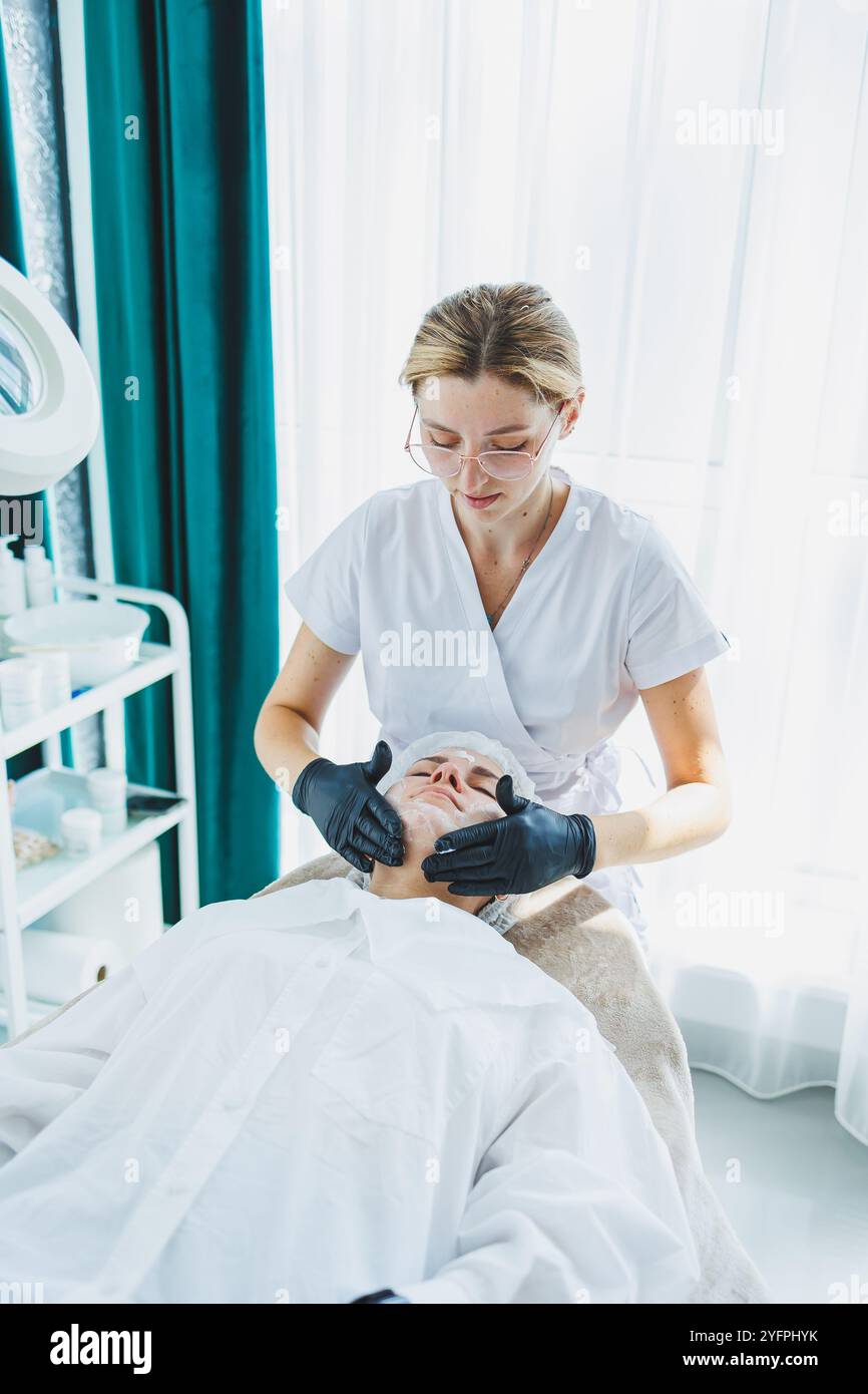 A smiling cosmetologist is doing a beauty procedure on her patient ...