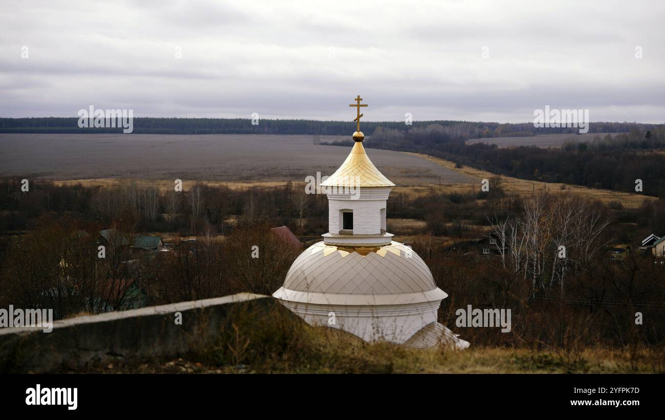 White orthodox church with golden roof and cross, standing on a hill ...