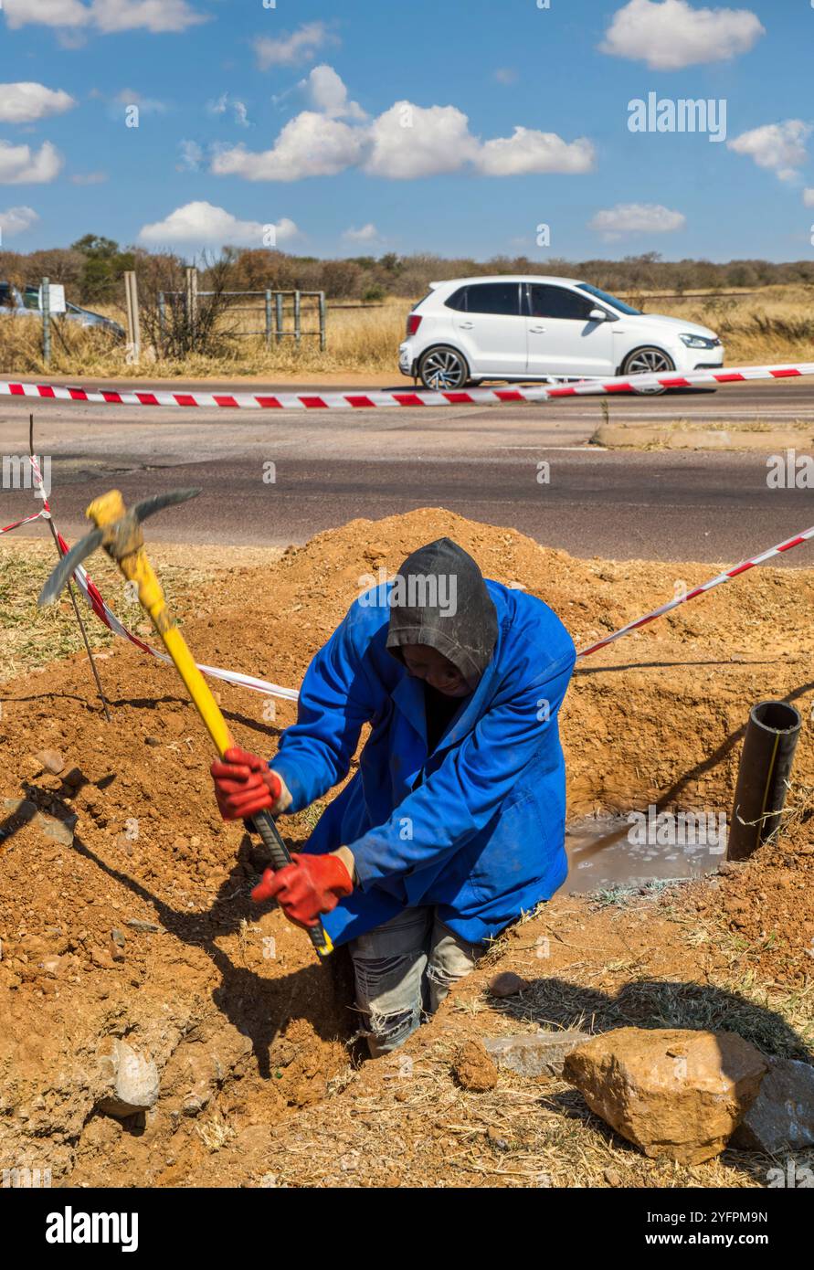 African worker with a pickaxe digging a trench on the side of the ...