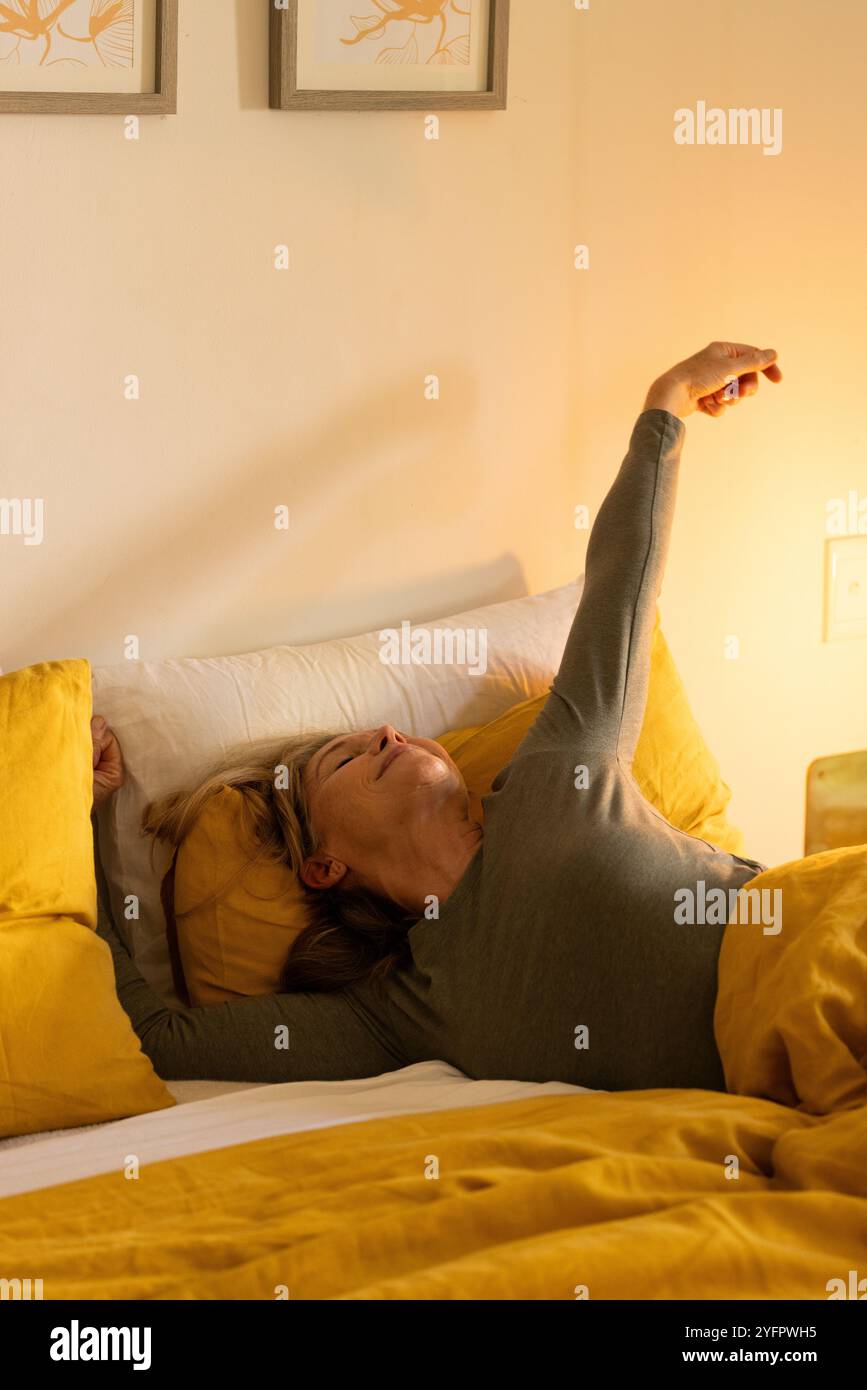 senior woman stretching in bed, waking up refreshed in cozy bedroom, at ...