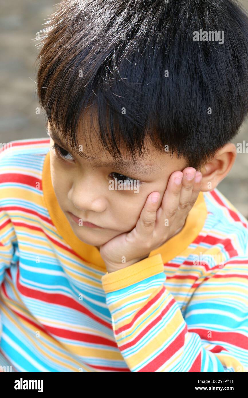 A thoughtful young boy in a colorful striped shirt displays a pensive ...