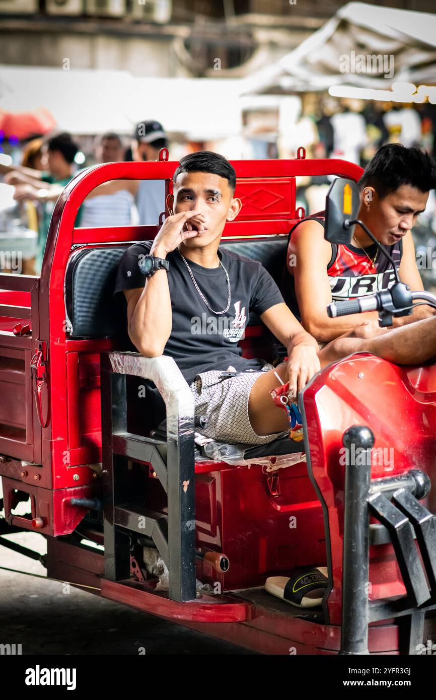 Two young filipino workers take a break sat on their jeep or trike in a ...