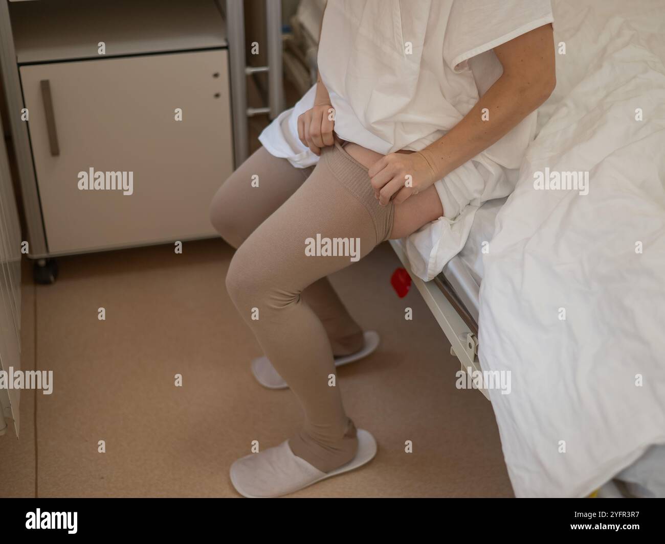 A woman puts on post-operative compression stockings in a hospital room ...