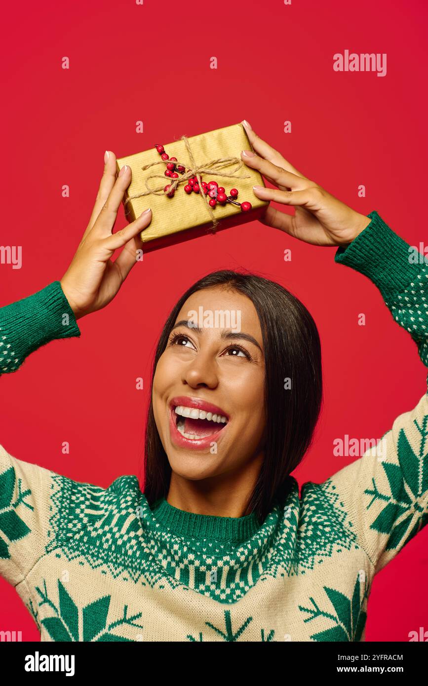 The young woman beams with happiness while lifting a wrapped gift high ...