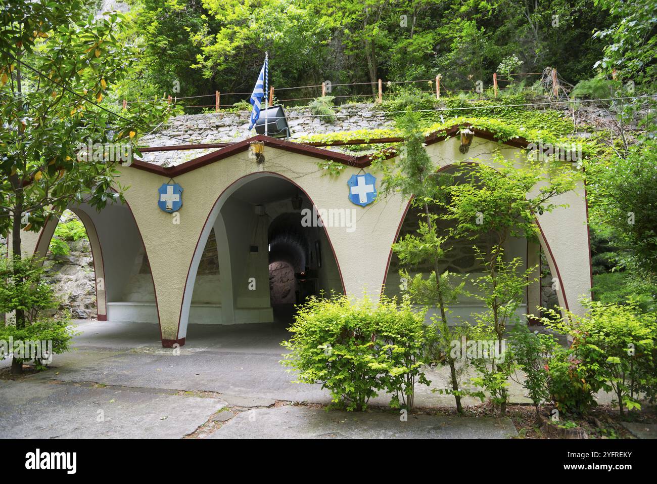 Entrance to a tunnel, surrounded by lush vegetation, with Greek flag ...