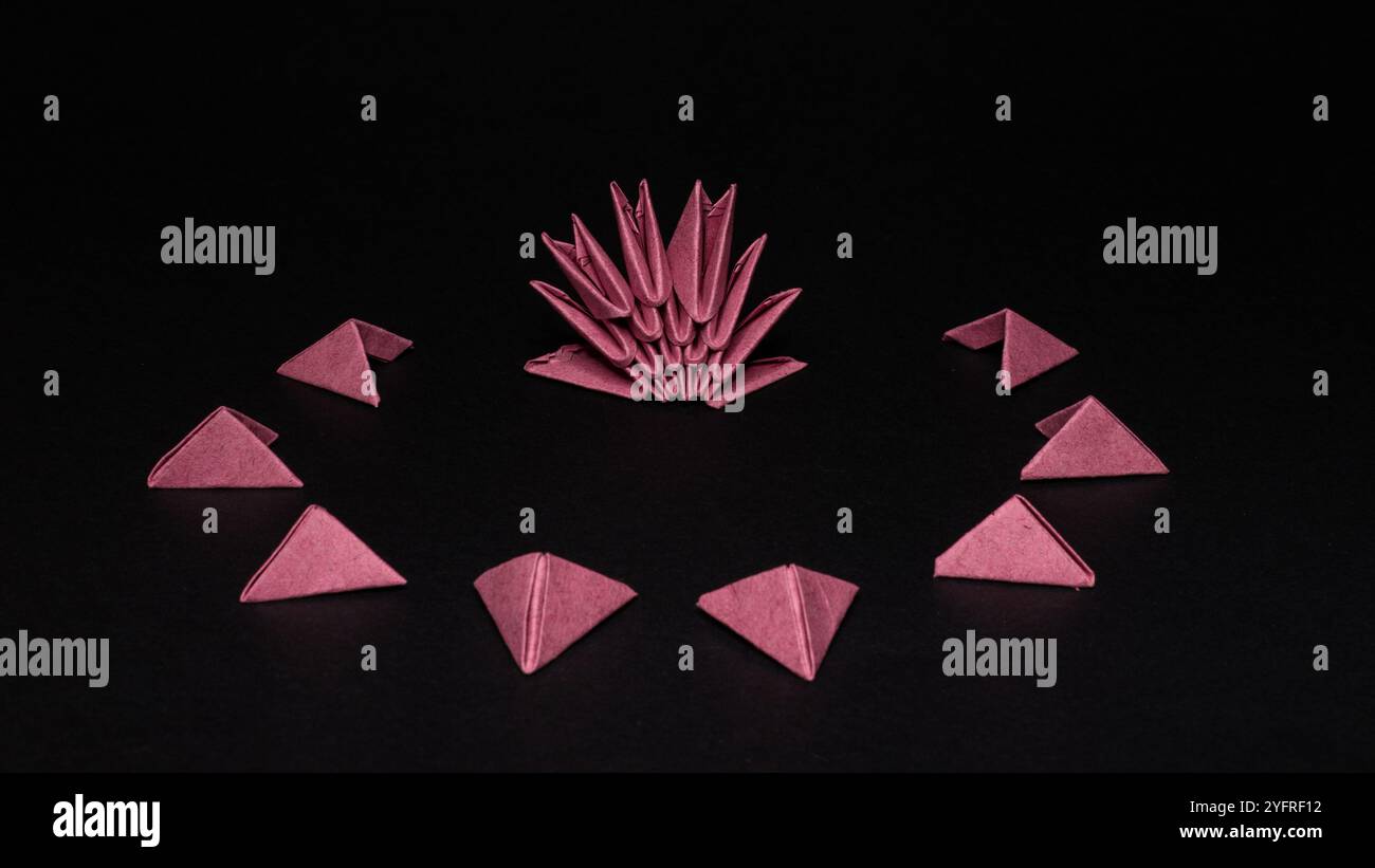 Pink origami watter lily surrounded by small origami paper pieces on a ...