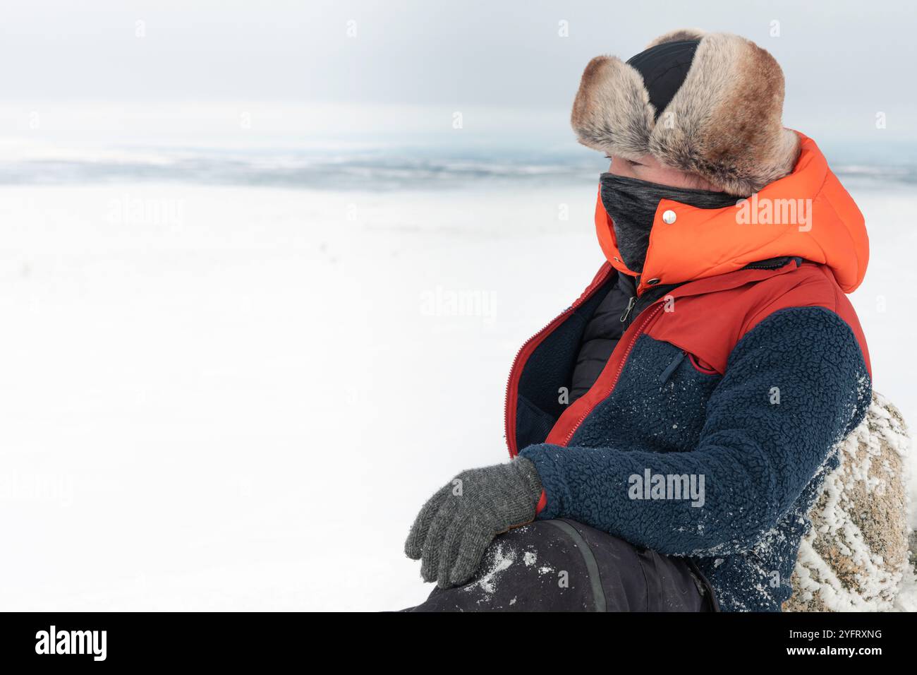 Adult caucasian male musher dressed in full arctic gear sitting on ...