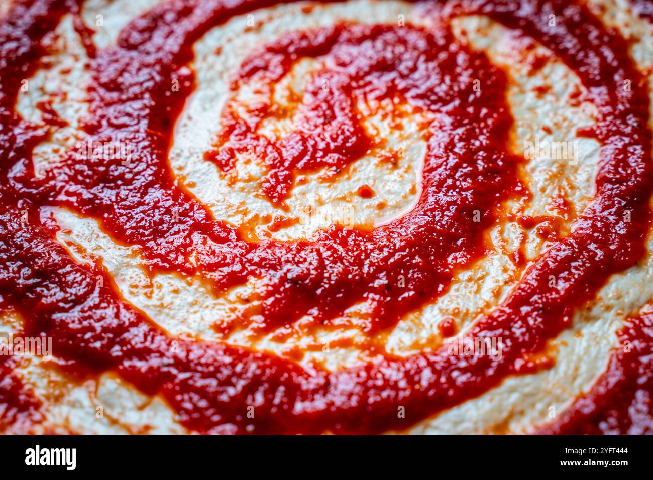 A circle of pizza dough is covered with tomato sauce in the form of a ...