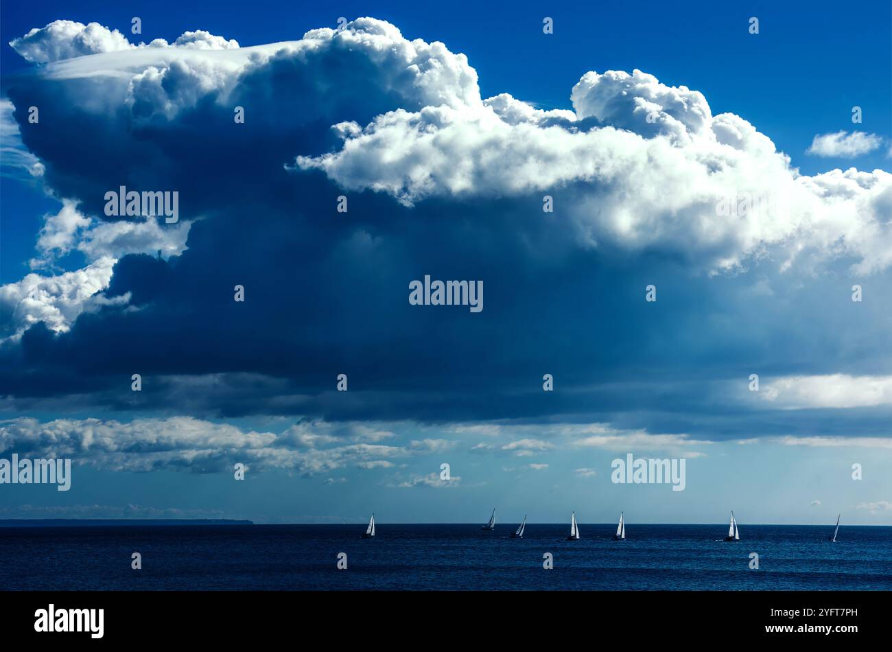 A cluster of sailboats sails peacefully on the tranquil ocean waters ...