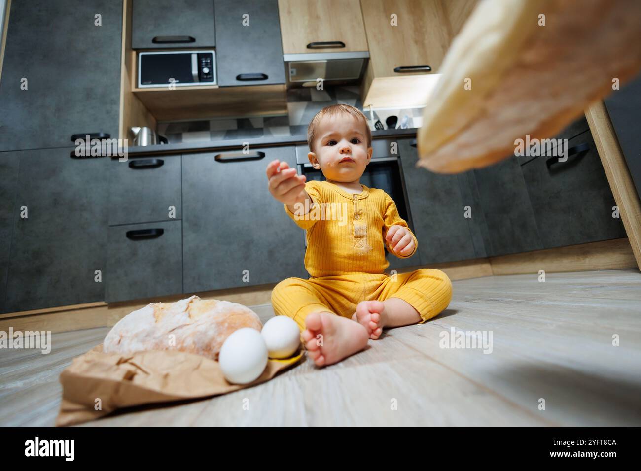 A little boy 1 year old is sitting in the kitchen with fresh bread ...