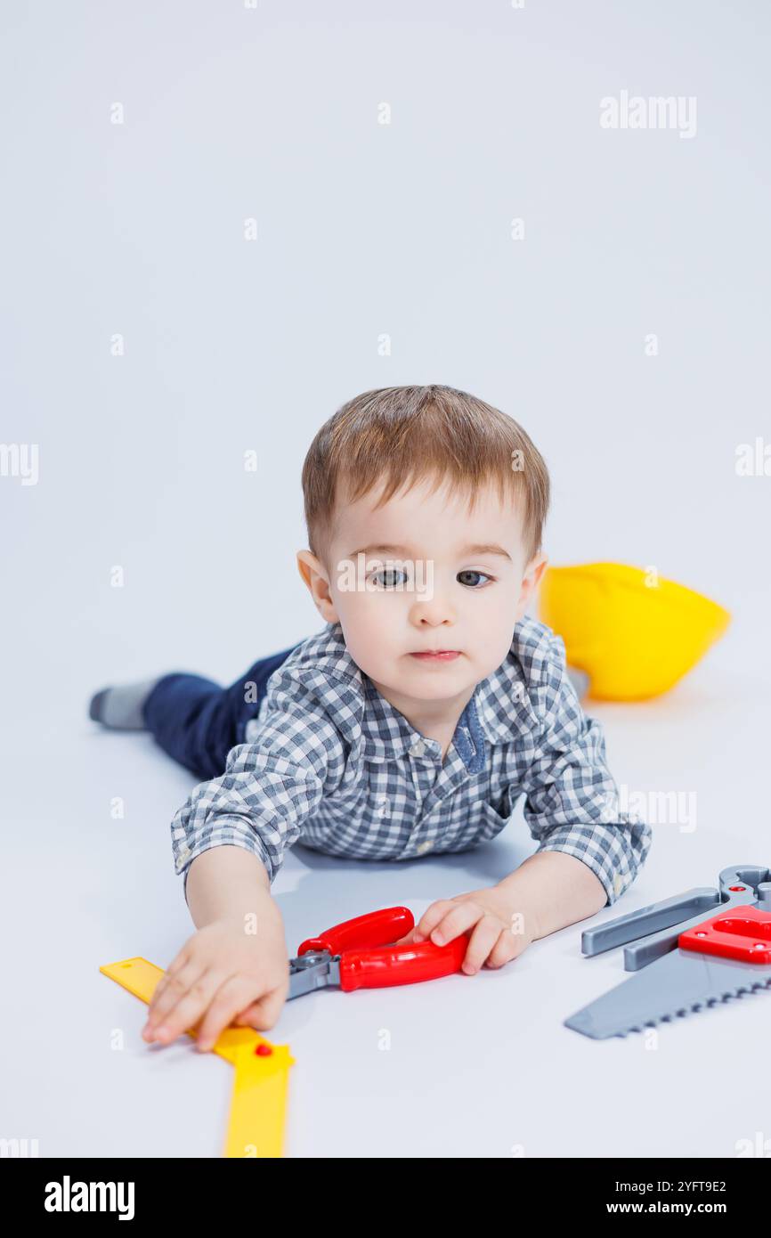 A little boy is playing with a toy set of builder's tools on a white ...