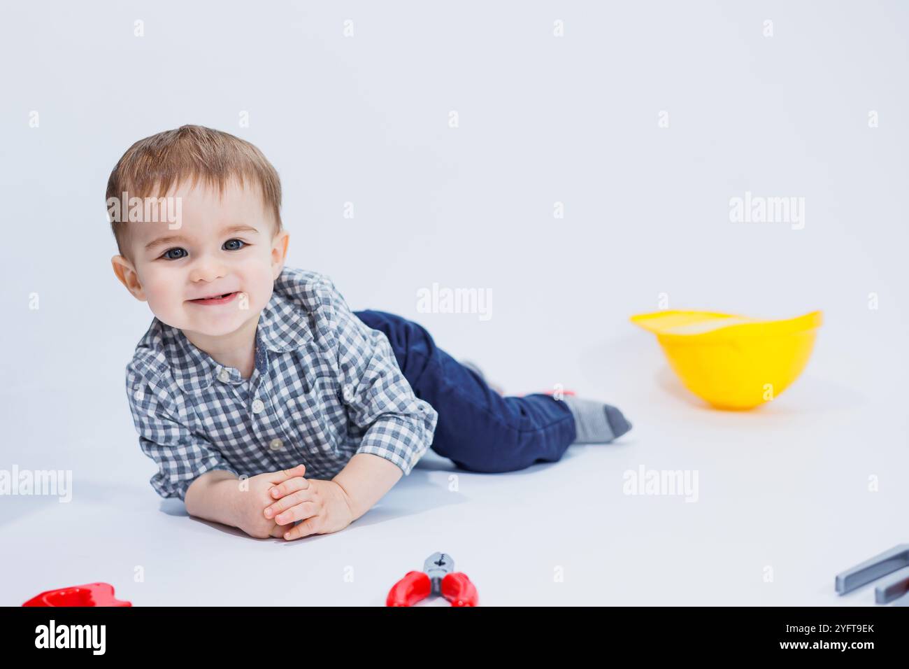 A little boy is playing with a toy set of builder's tools on a white ...