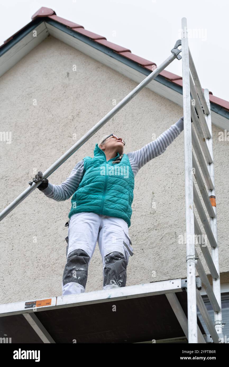 Gerüstbauerin, Malerin baut ein mobiles Gerüst am Einfamilienhaus auf ...