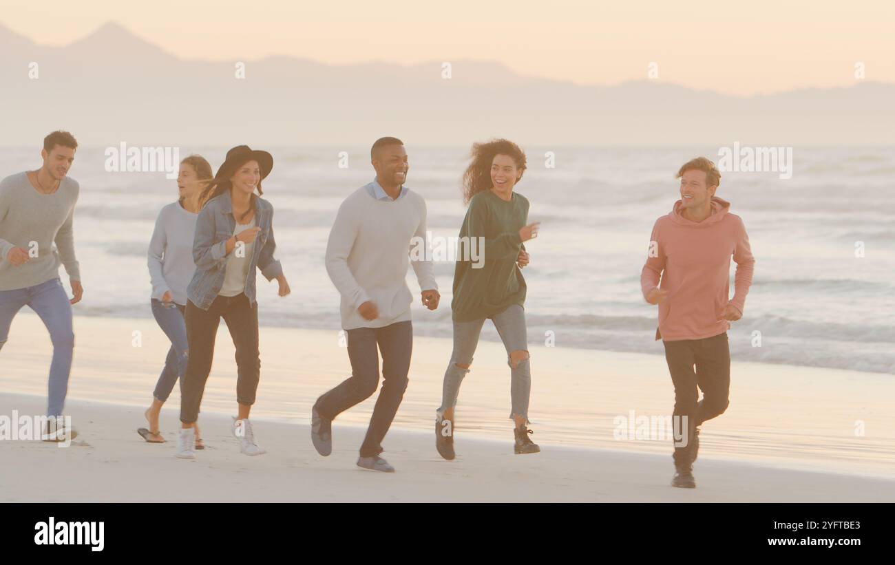 Group Of Casually Dressed Friends Having Fun Running Along Winter Beach ...