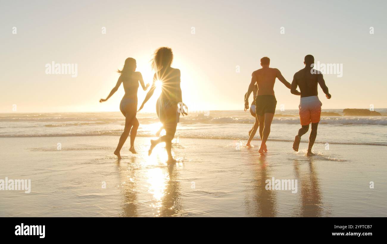 Group Of Friends In Swimwear Run Through Waves At Sunset On Summer ...