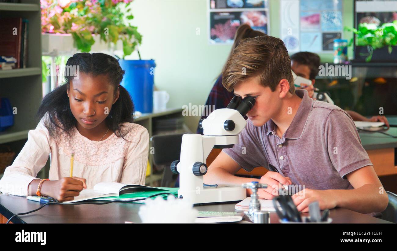 High School Students Looking Through Microscope And Writing Notes In ...