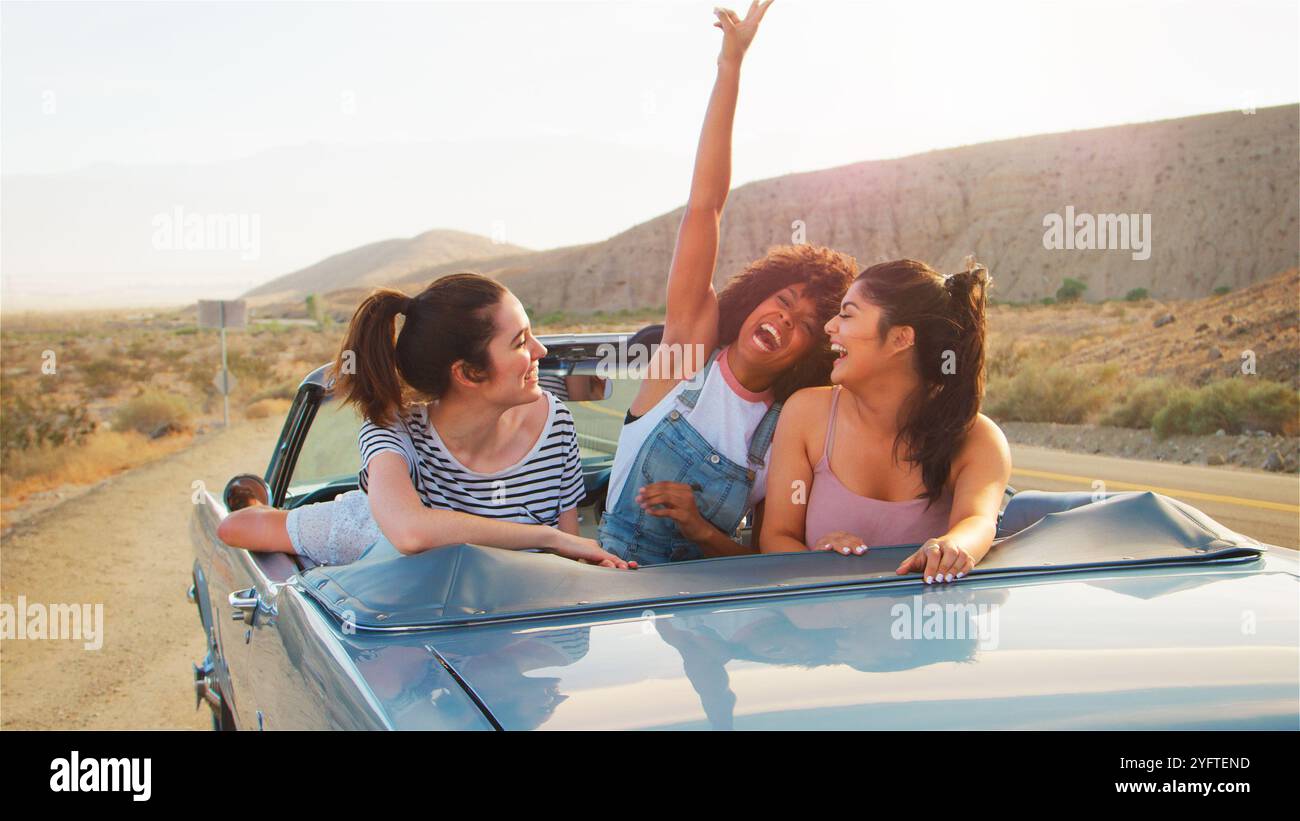 Three Female Friends In Back Seat Of Classic Open Top Car On Road Trip ...